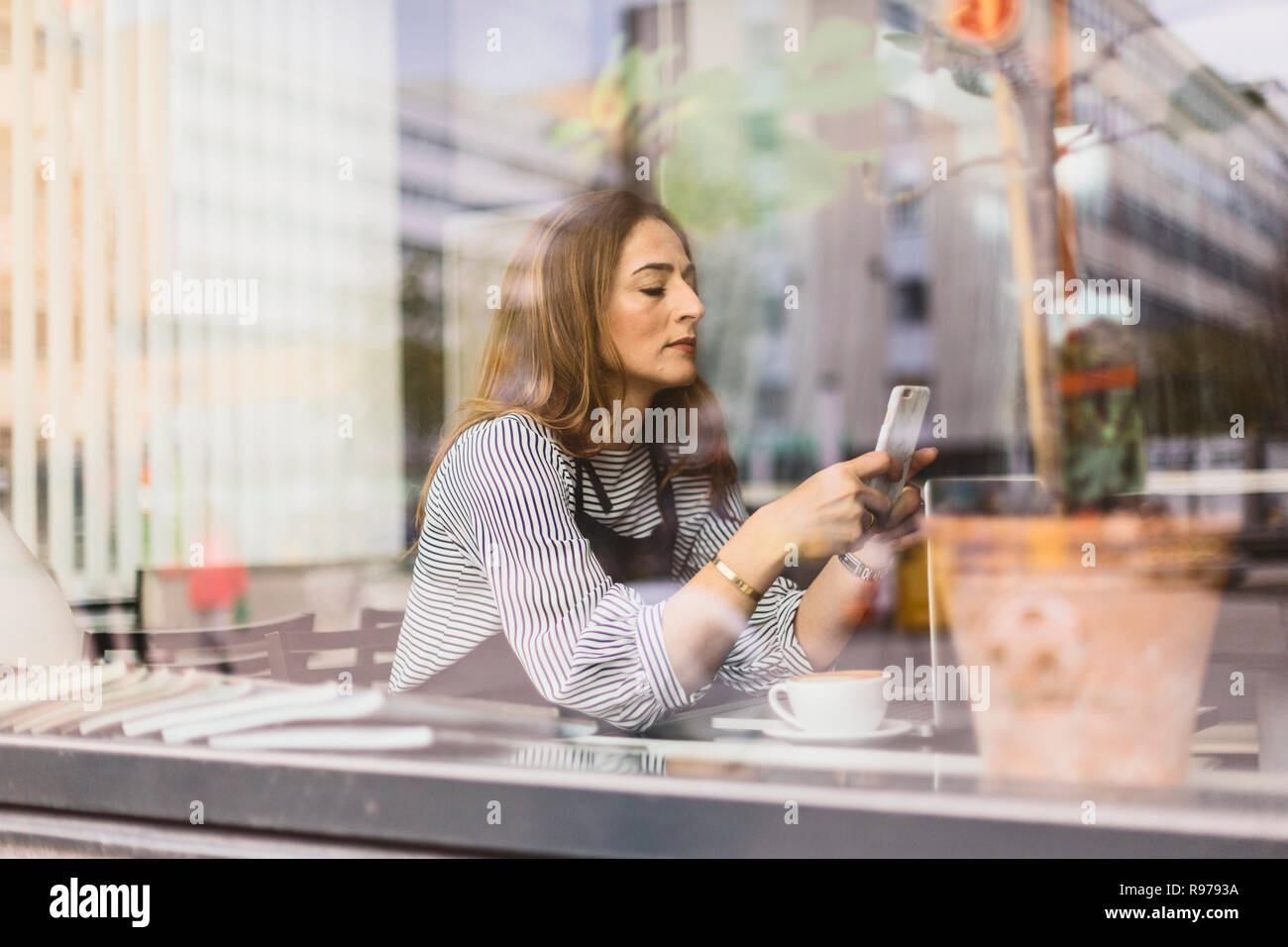 Barista using smart phone behind cafe window Stock Photo - Alamy