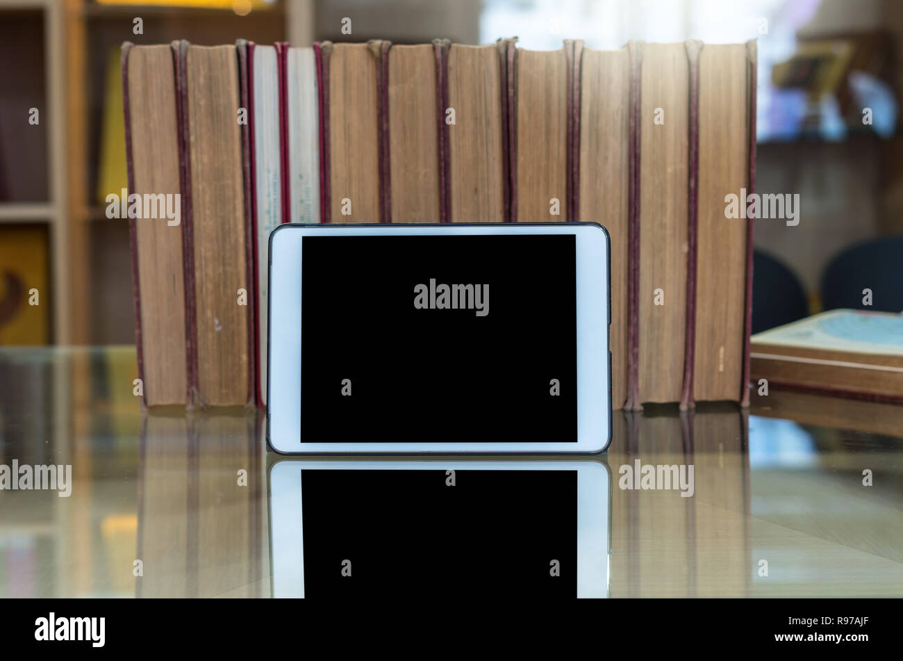 Tablet with old book on the glass table in library Stock Photo - Alamy