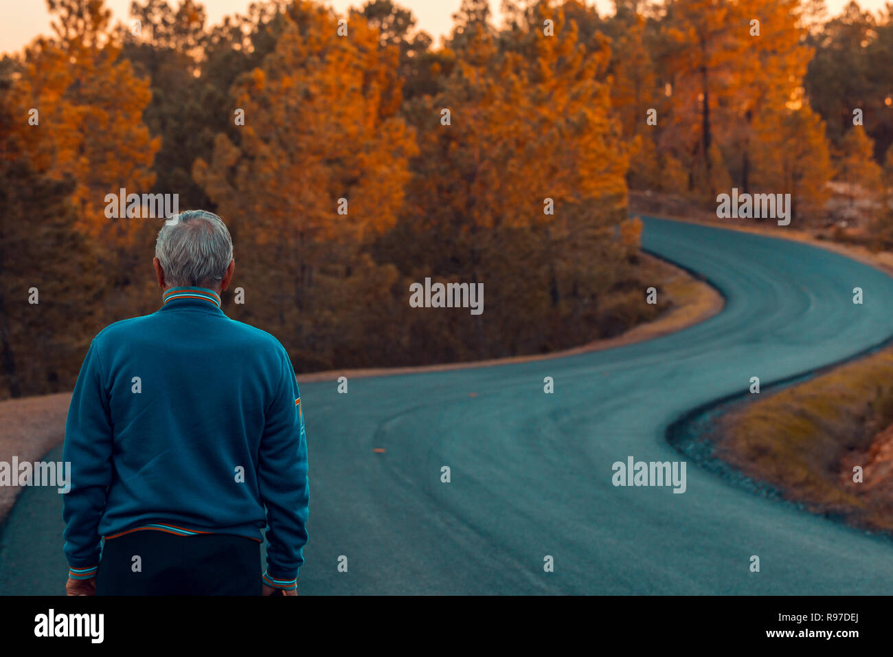 Active senior man stands alone on lonely road between mountains. Older ...