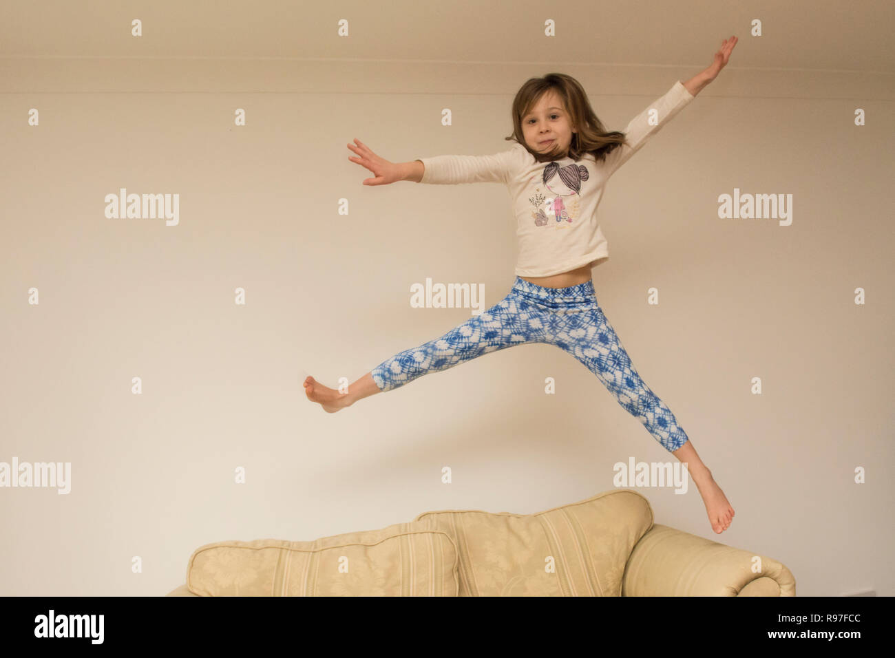 child, girl indoors leaping, jumping on furniture, sofa, being ...