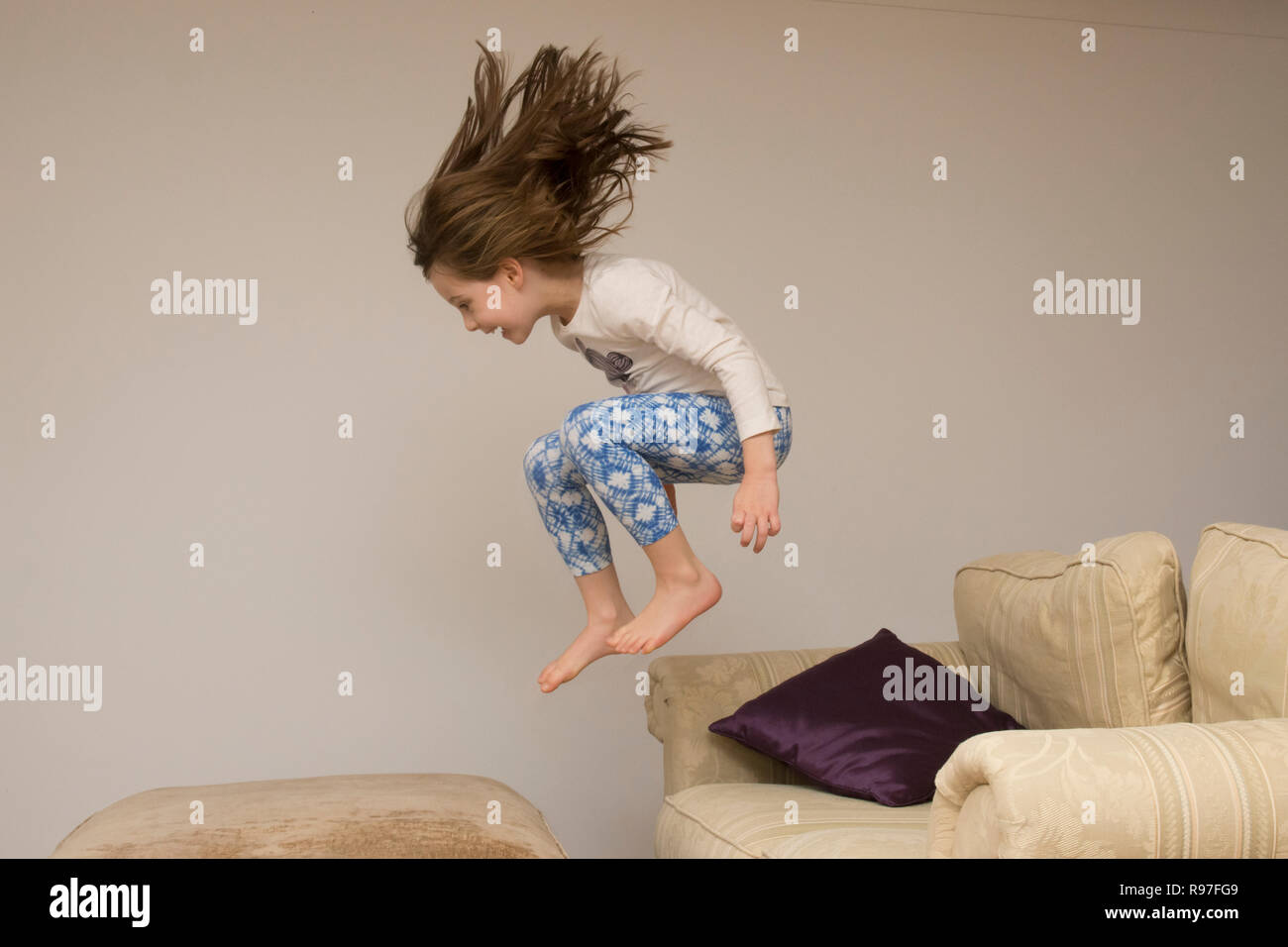 child, girl indoors leaping, jumping on furniture, sofa, being ...