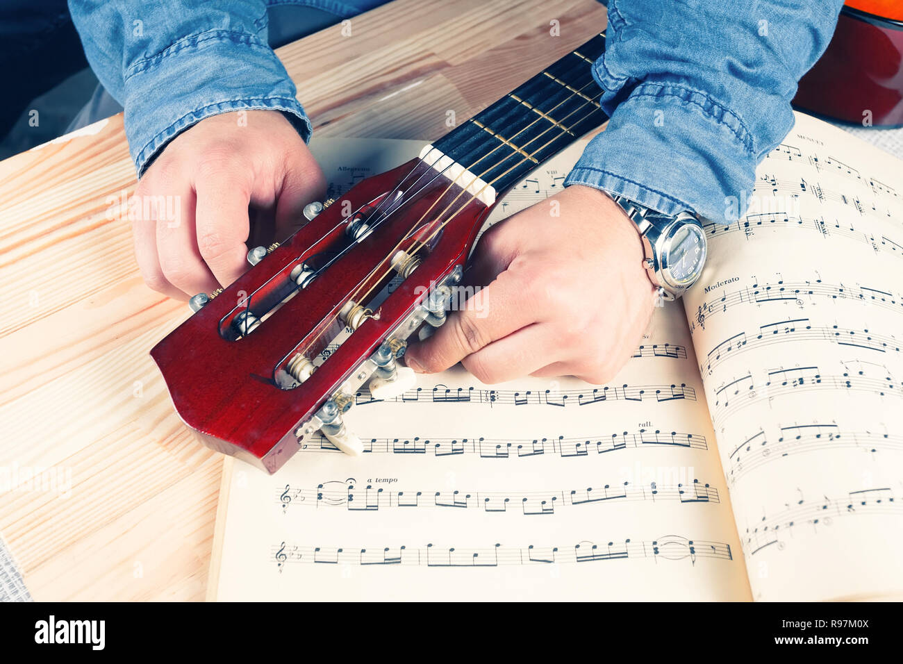 Young man tuning a guitar. Head and pegs. Music notes. Light wooden ...