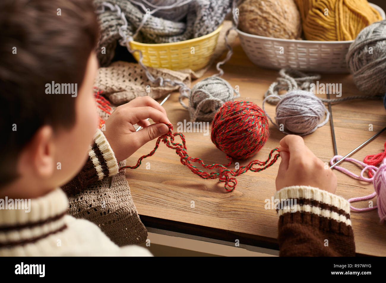 Child boy is learning to knit. Colorful wool yarns are on the wooden ...