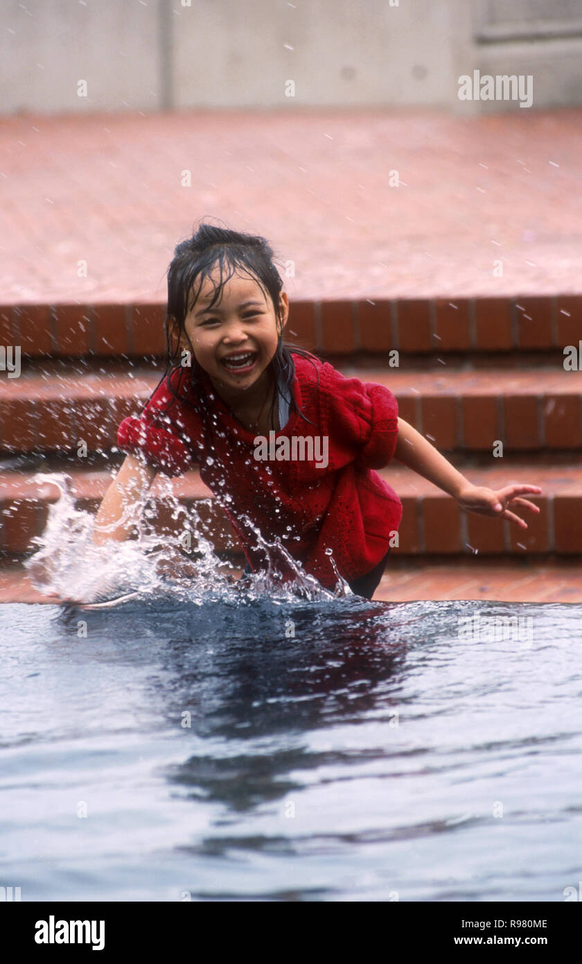 A YOUNG ASIAN GIRL COOLING OFF AND HAVING FUN IN A FOUNTAIN AND POND IN ...