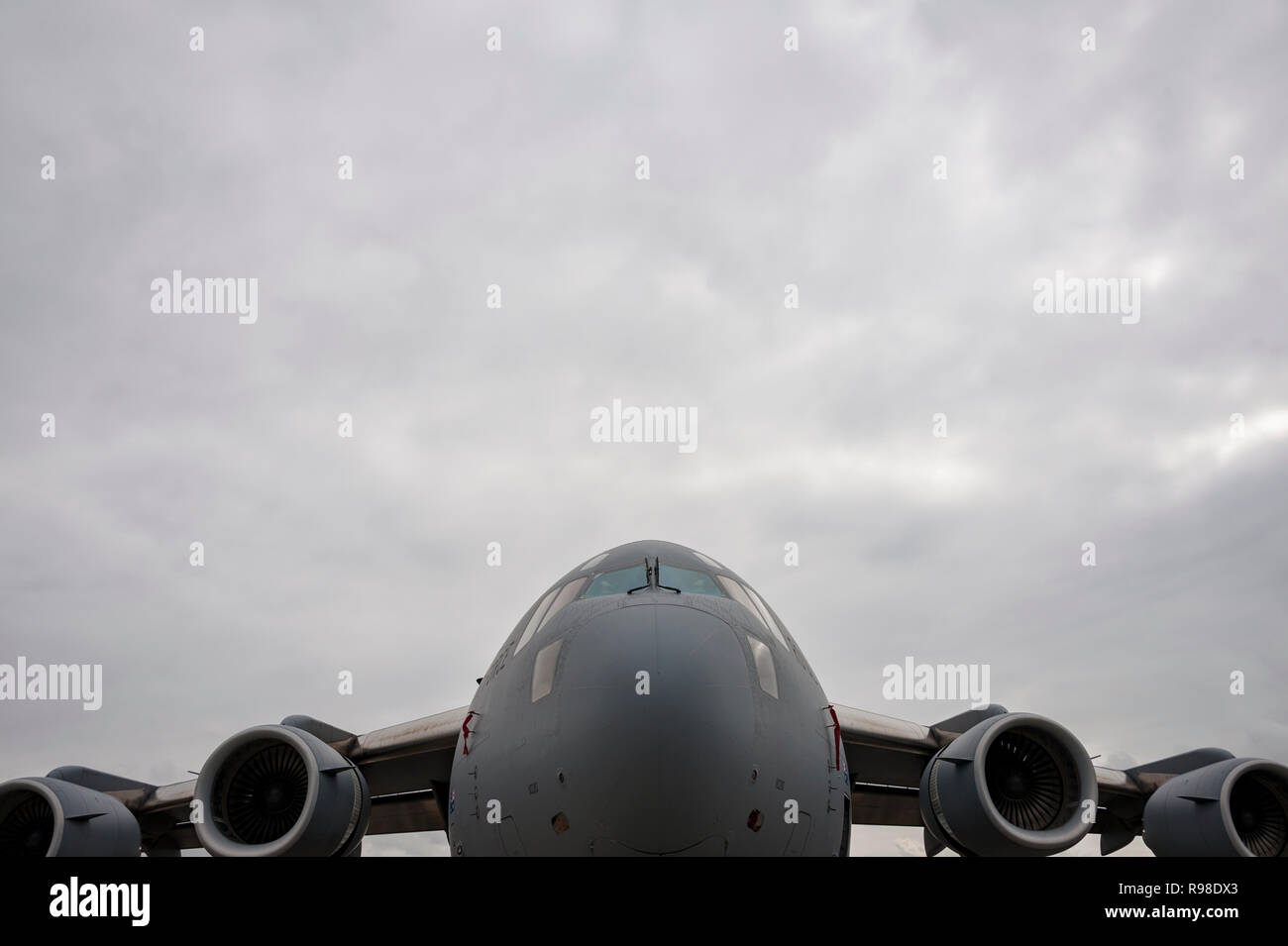 Modern military cargo jet, low and symmetrical in frame with cloudy sky ...