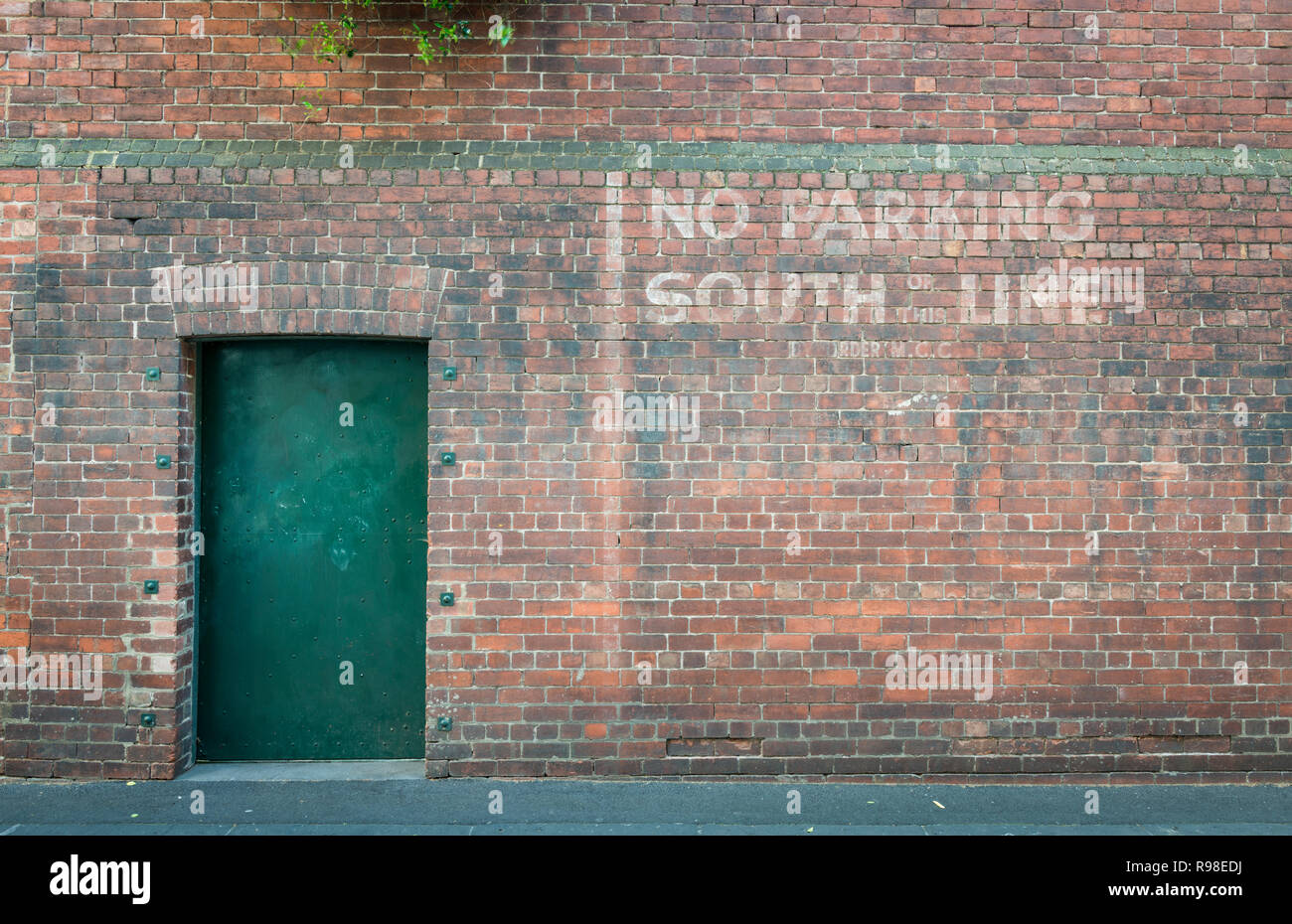 Old no parking sign fading into the brick wall, with green door Stock ...