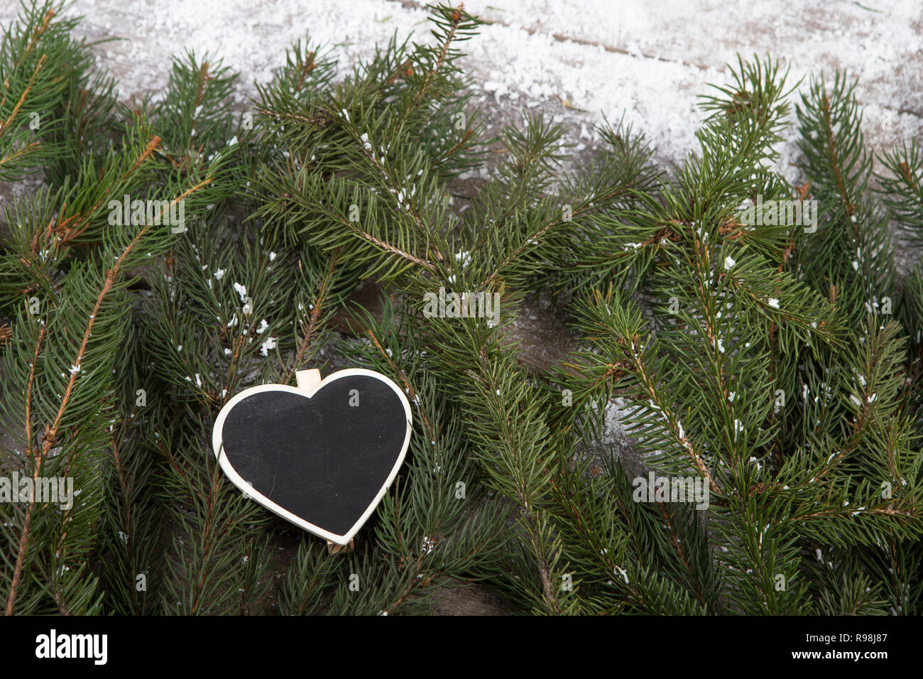 Blackboard in heart shape, fir branches on a snow-covered wooden ...