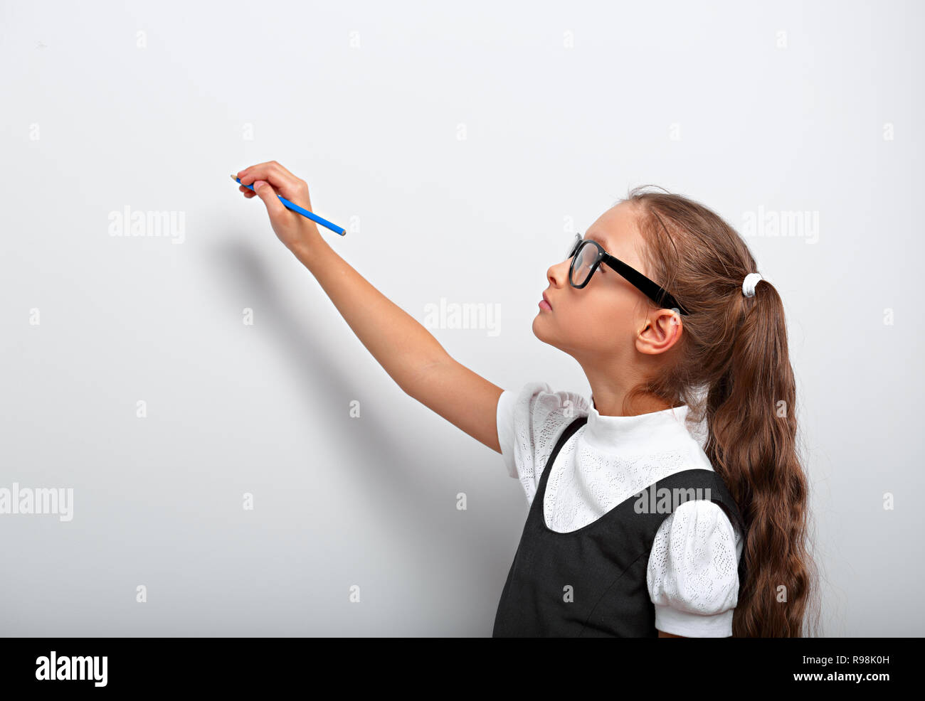 Smart pupil kid girl in eyeglasses looking up on the blue wall ...