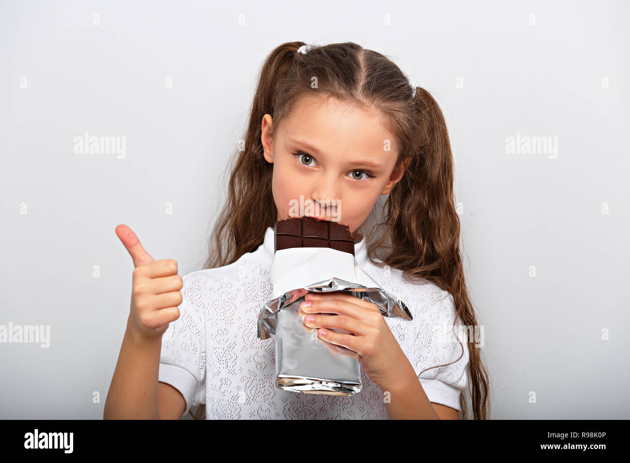 Happy fun smiling kid girl biting dark chocolate and showing thumb up ...