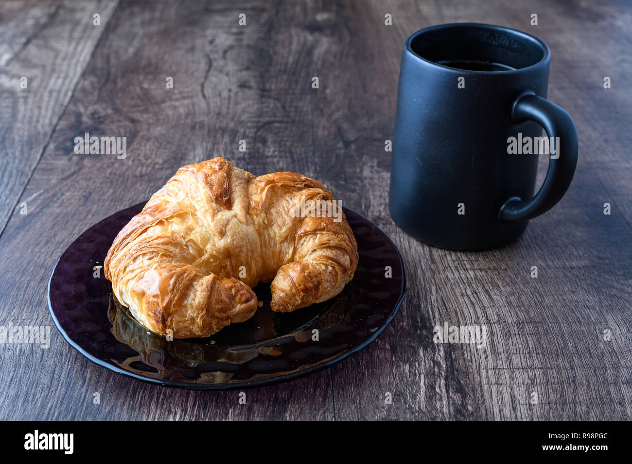 Fresh croissant on a purple glass plate on a wood table top with black ...