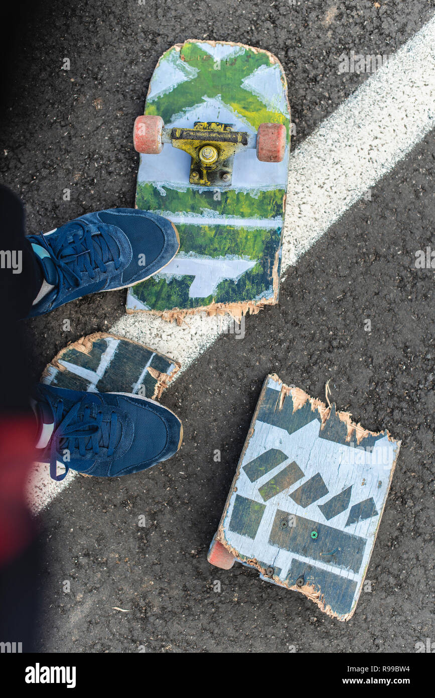 Broken skateboard on dark asphalt street. Boy with sneakers stepped on ...