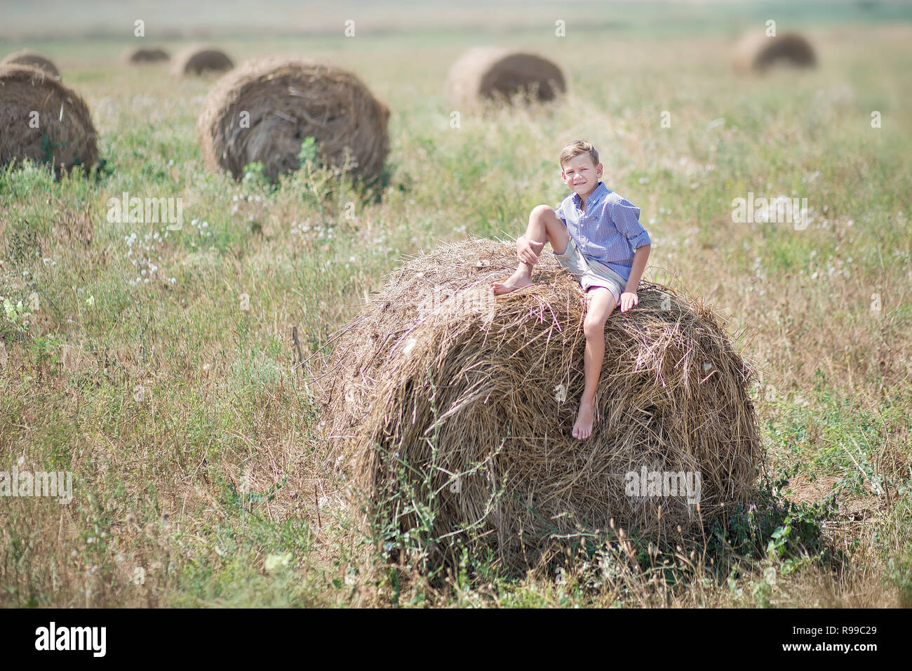 Attractive boy sitting on a haystack and smiling Stock Photo - Alamy
