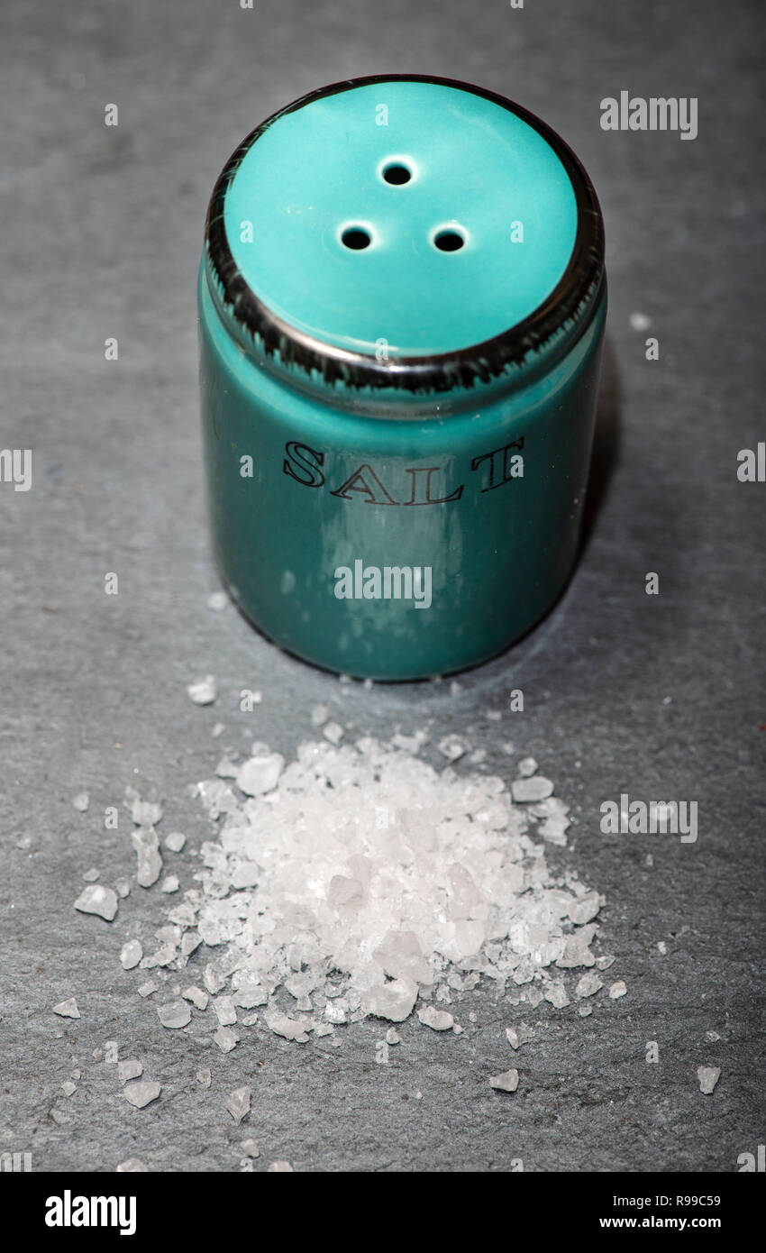Salt shaker and grinded salt on stone dark table. Pieces white salt ...