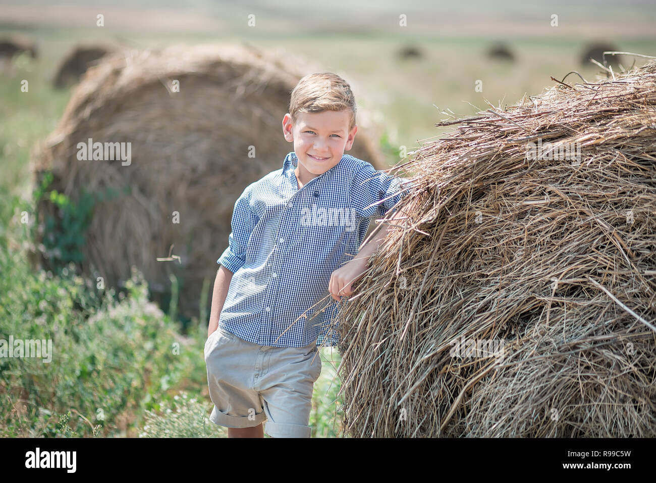 Attractive boy sitting on a haystack and smiling Stock Photo - Alamy