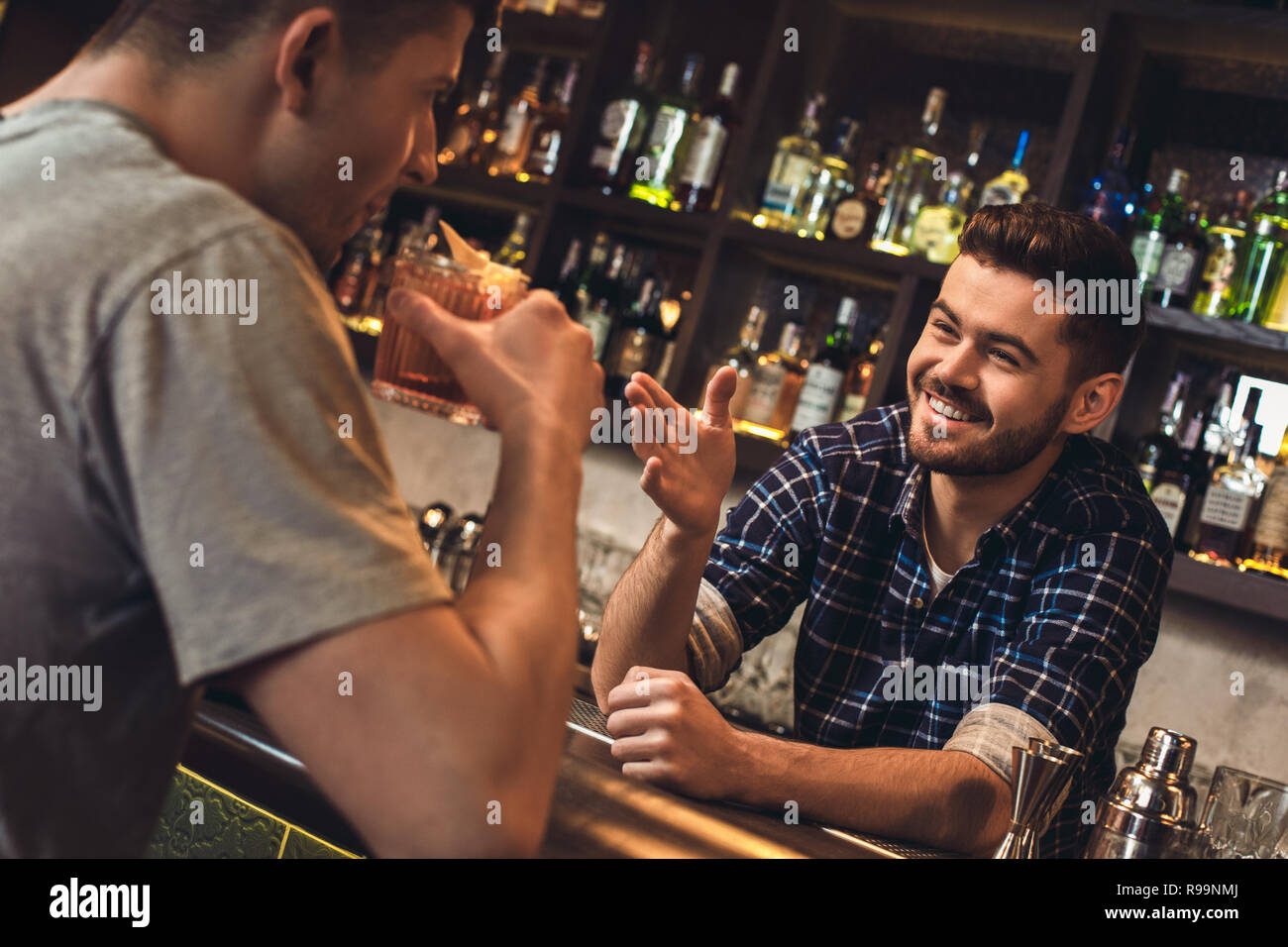 Young barman standing at bar counter talking with customer drinking ...