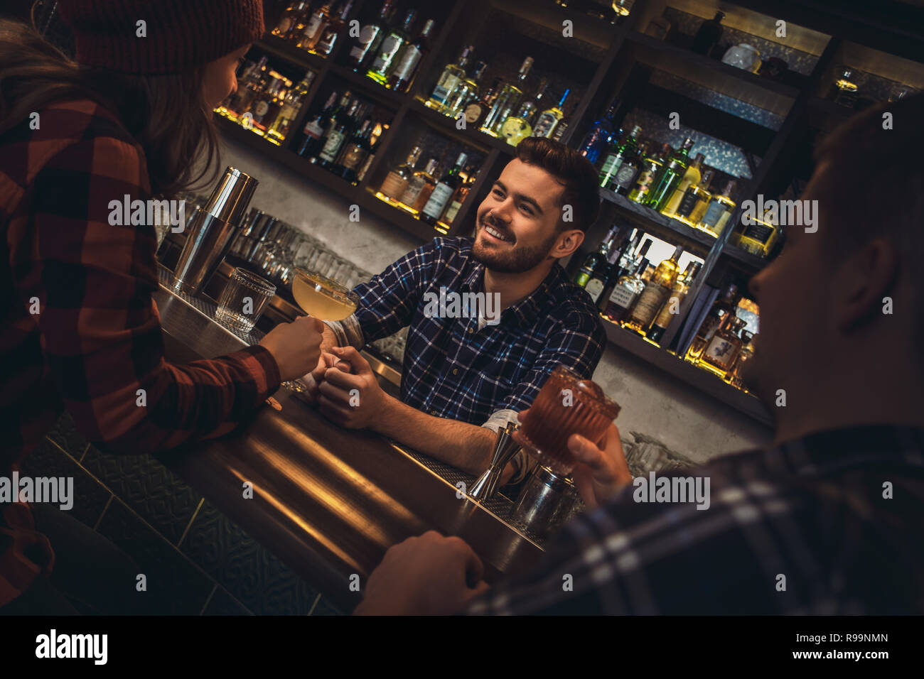 Young barman standing at bar counter with visitors drinking cocktails ...