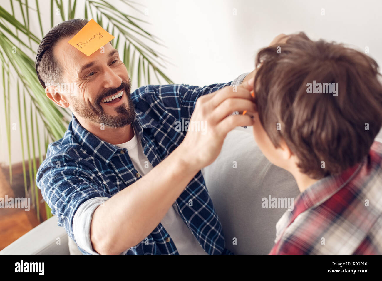 Father and little son together at home sitting on sofa playing forehead ...