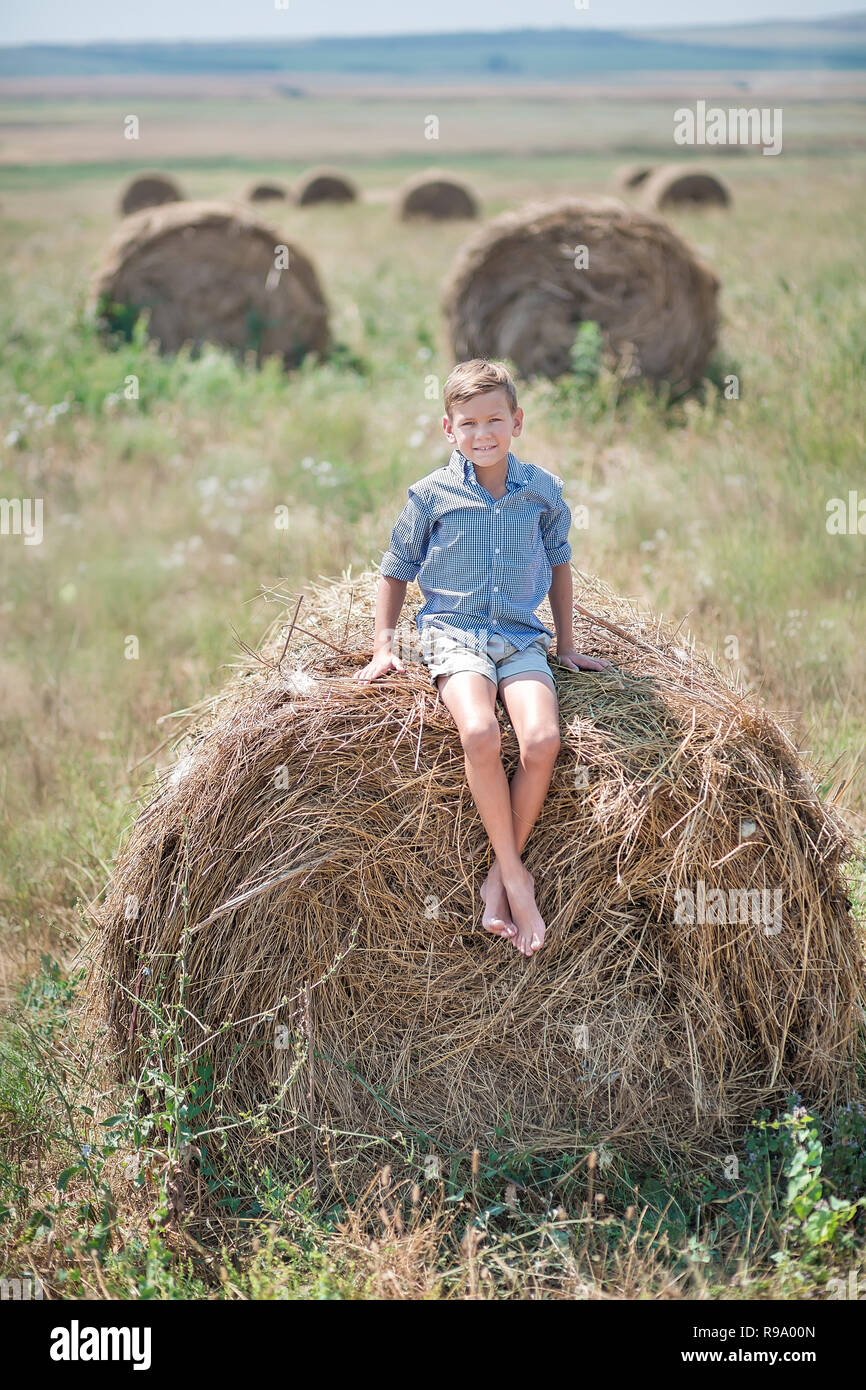 Attractive boy sitting on a haystack and smiling Stock Photo - Alamy