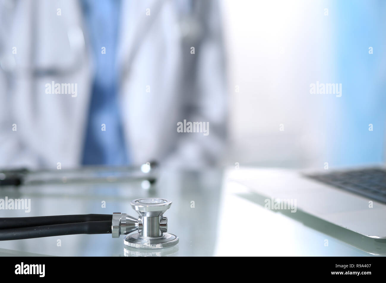 Stethoscope lying on glass desk with laptop computer at busy physician ...