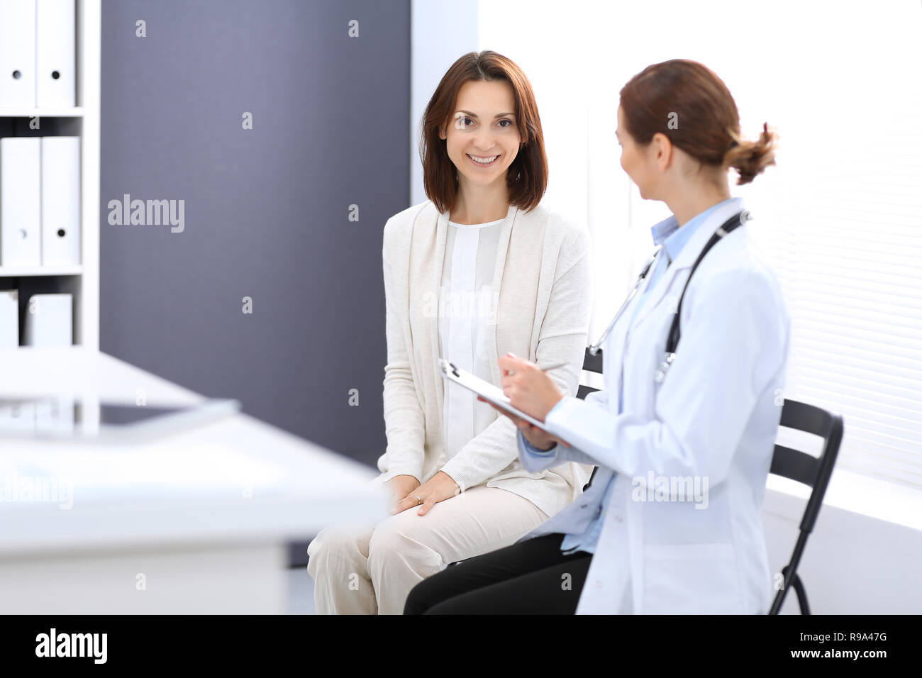 Happy doctor and patient discussing something while sitting at the ...