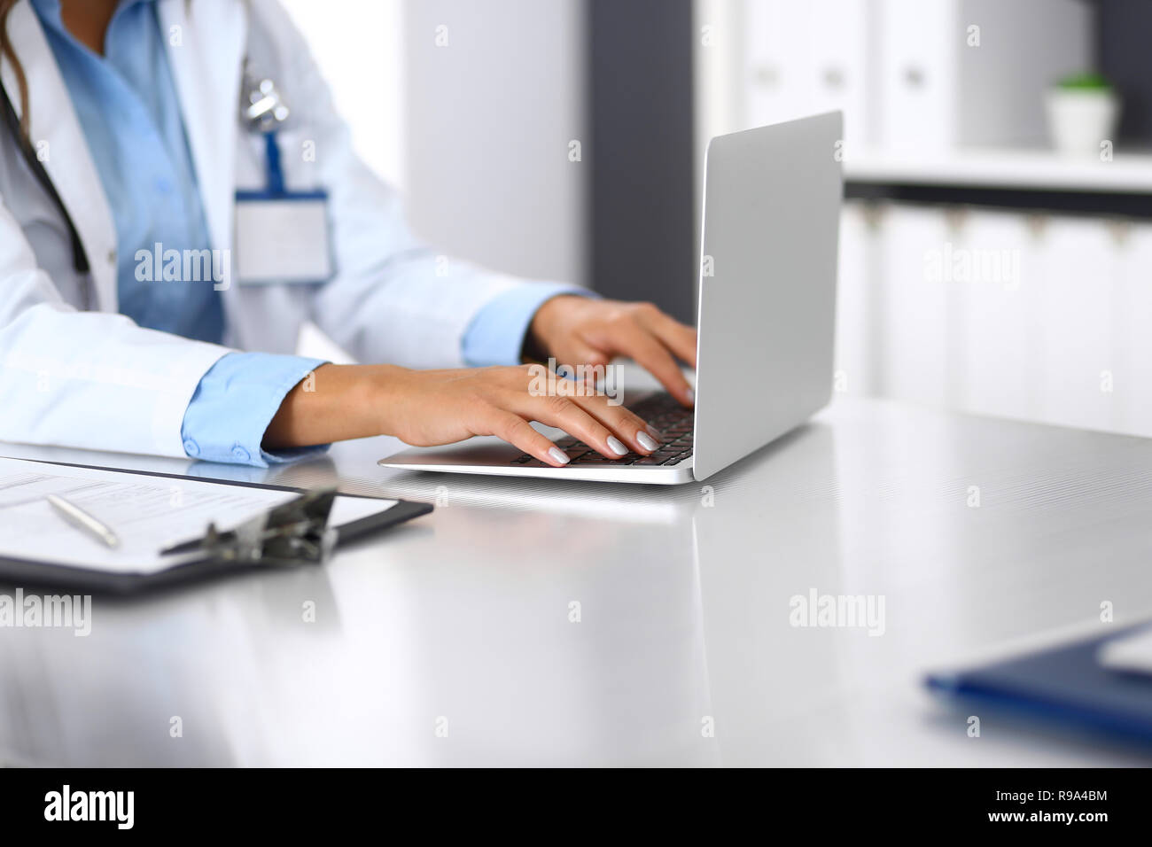 Unknown doctor woman typing on laptop computer while sitting at the ...