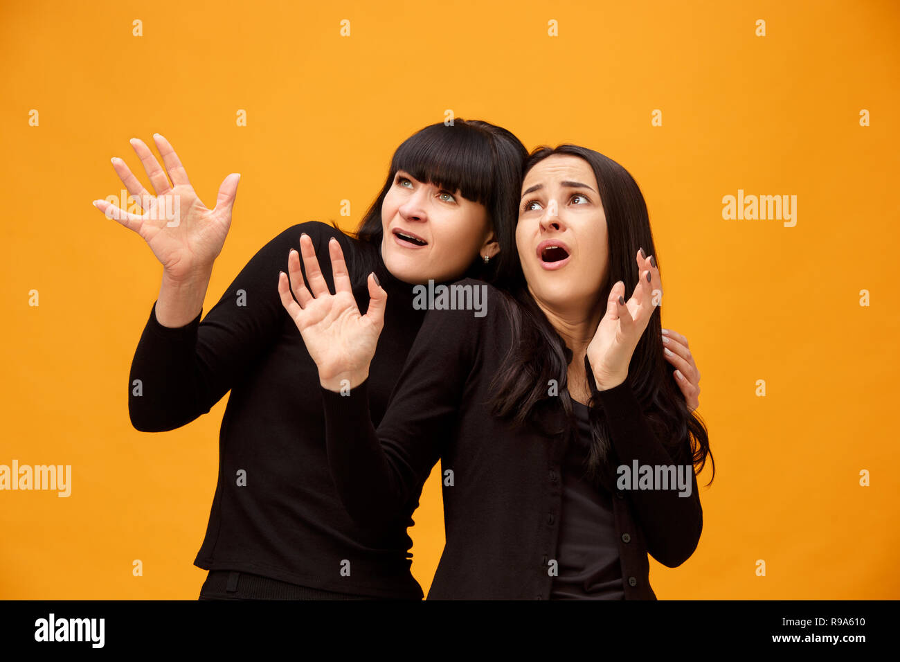 A portrait of a scared mother and daughter at studio on gold background ...
