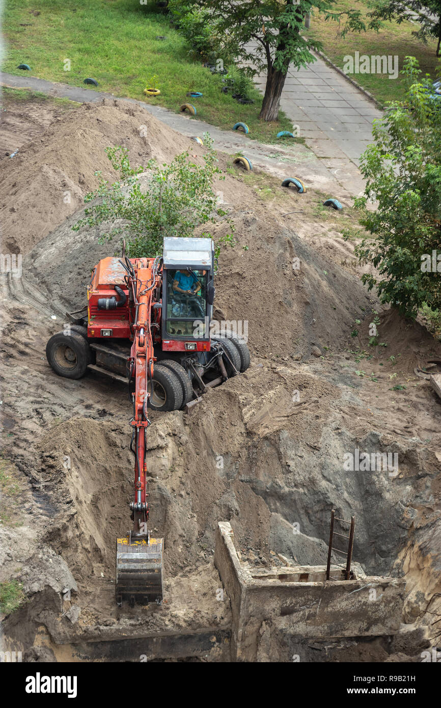 Red excavator digging a pit. Repair of water pipes Stock Photo - Alamy