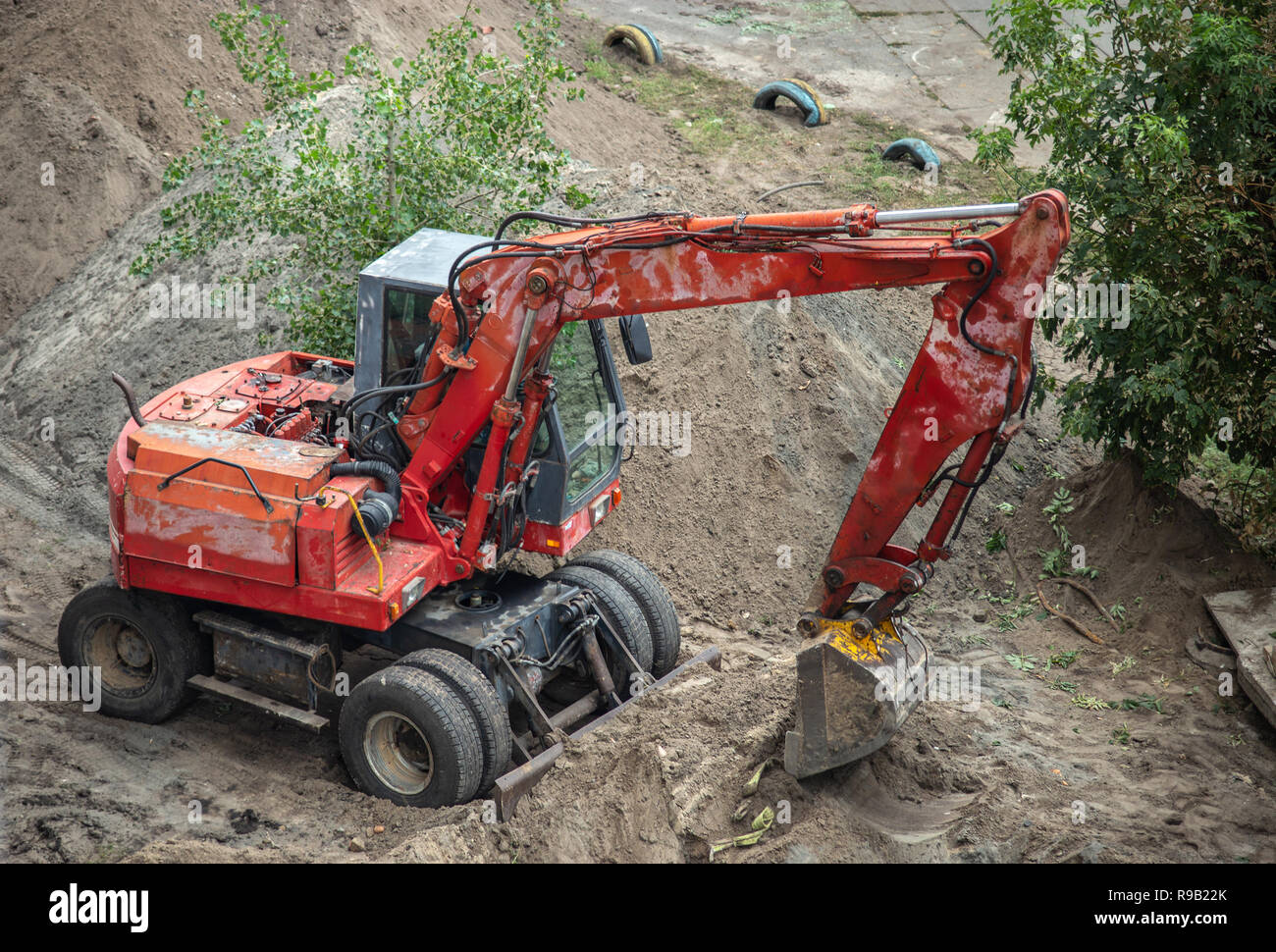 Red excavator digging a pit. Repair of water pipes Stock Photo - Alamy