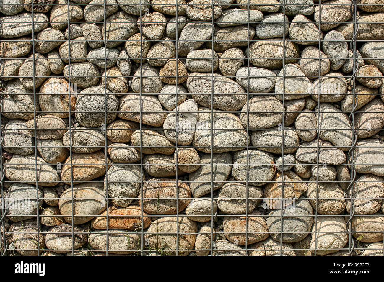 Wall made of round rocks, secured with steel wire net (iron stone ...