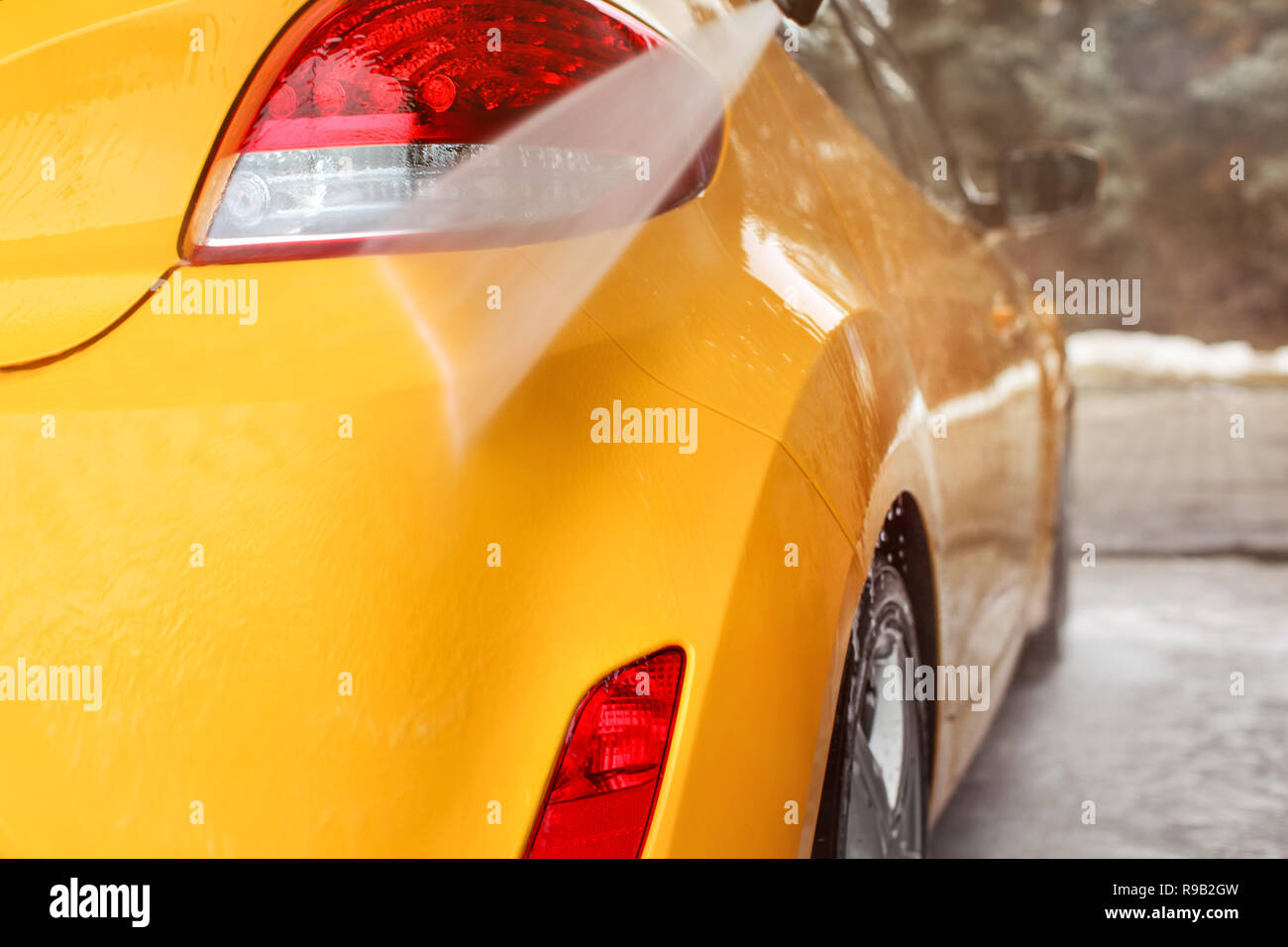 Yellow car rear light and bumper washed in self serve carwash, water ...