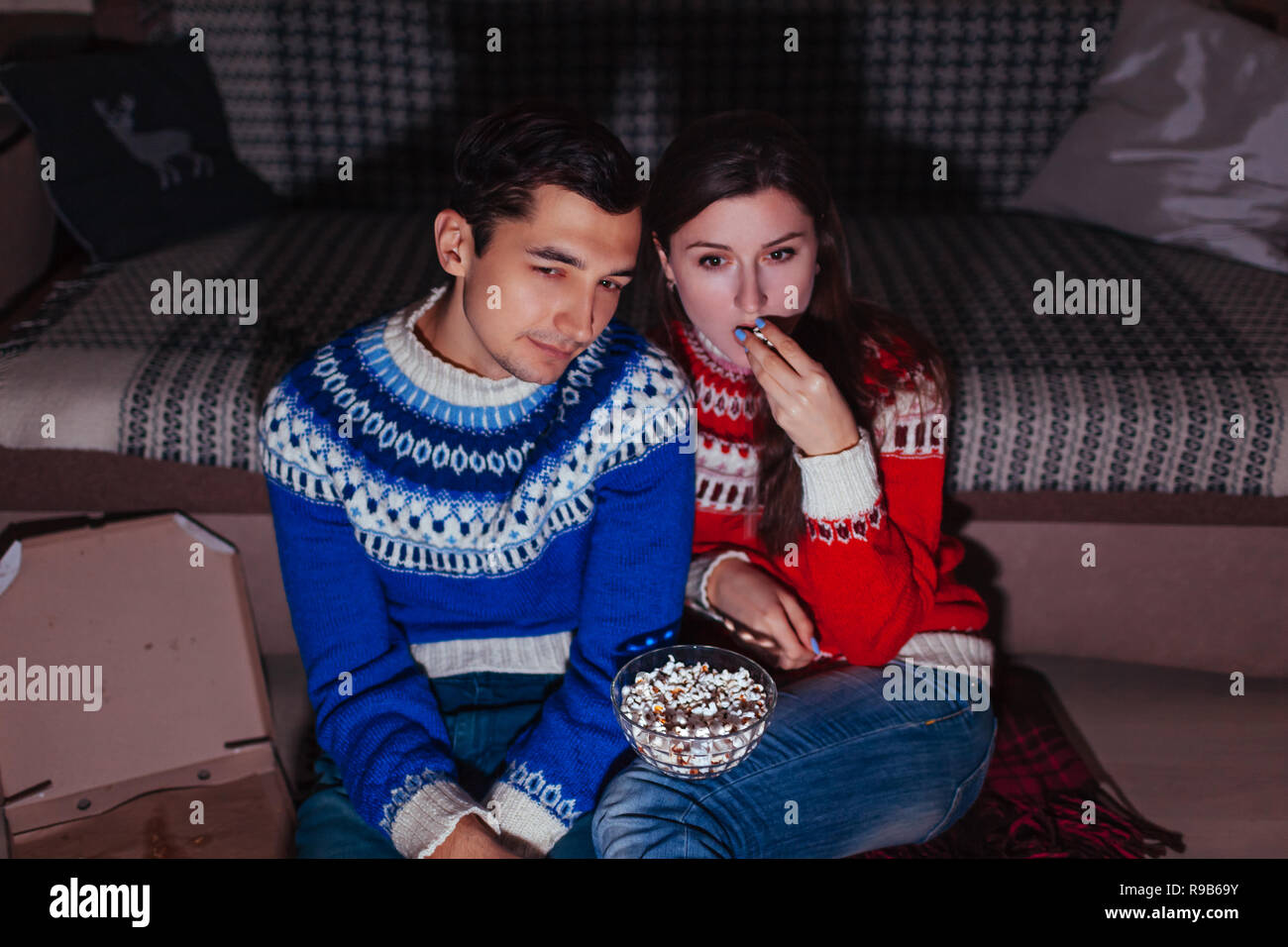 Young couple watching horror movie eating popcorn at home at night ...