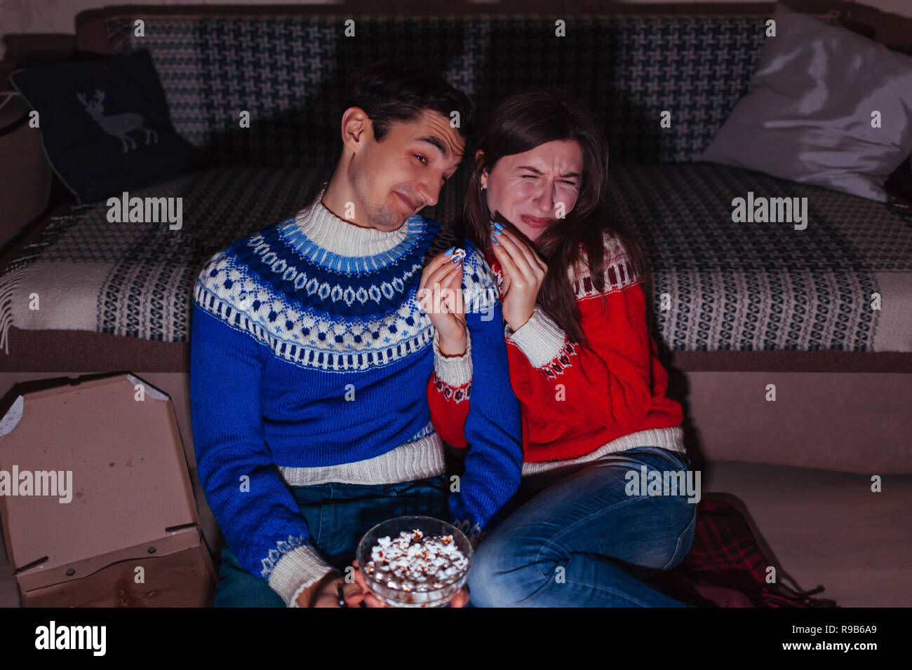 Young couple watching horror movie eating popcorn at home at night ...