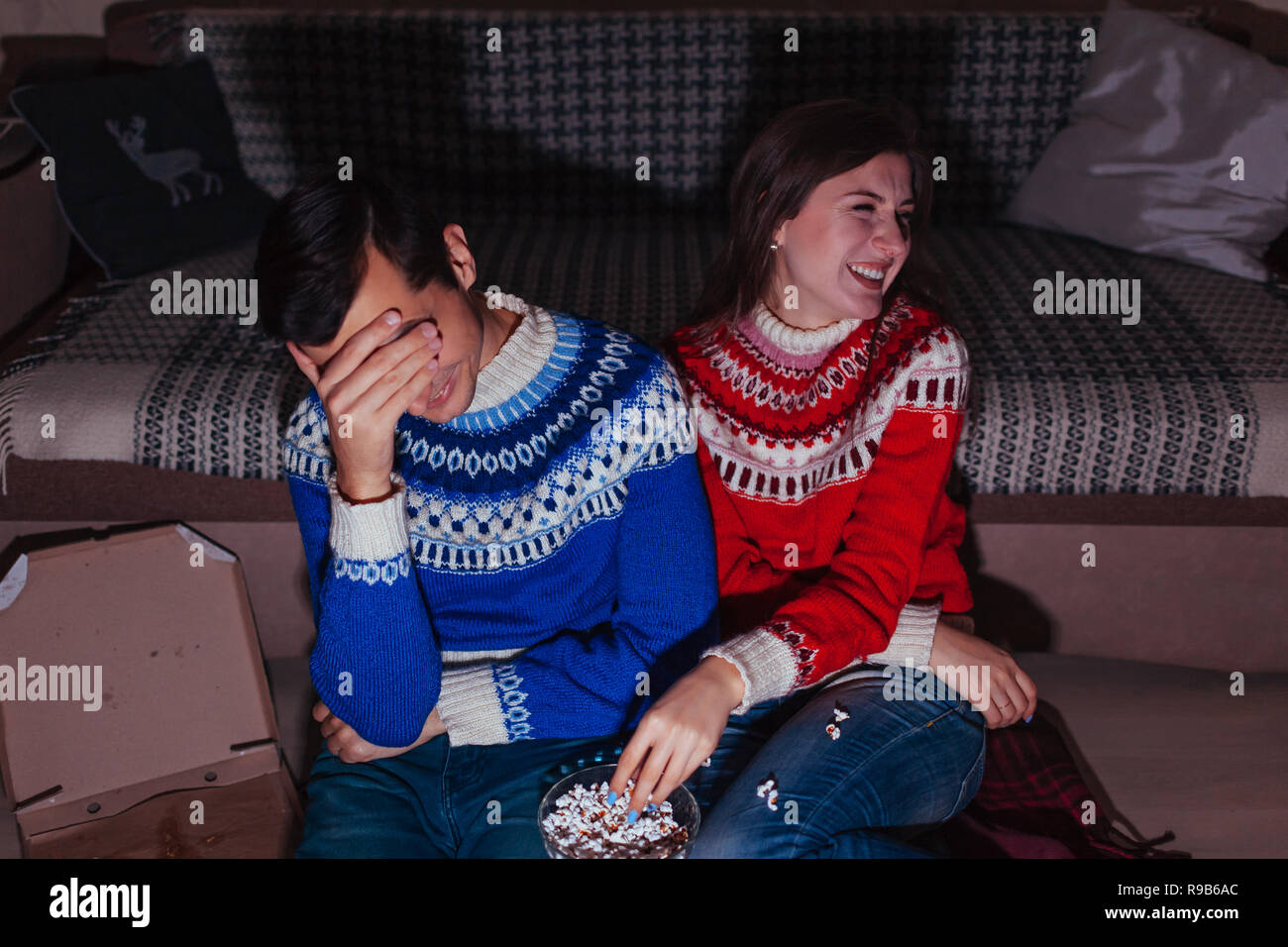 Young couple watching comedy movie eating popcorn at home at night ...