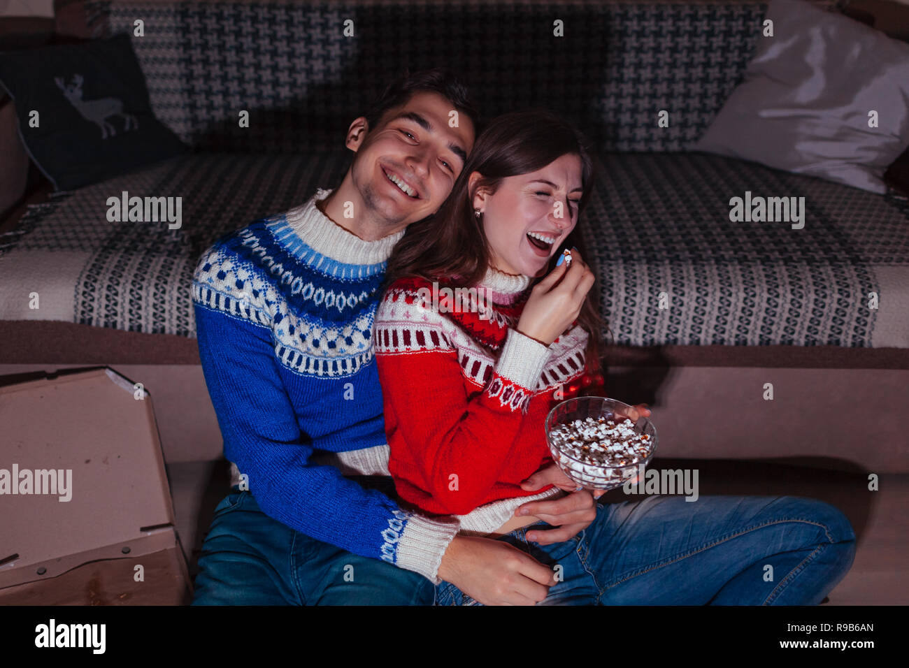 Young couple watching comedy movie eating popcorn at home at night ...