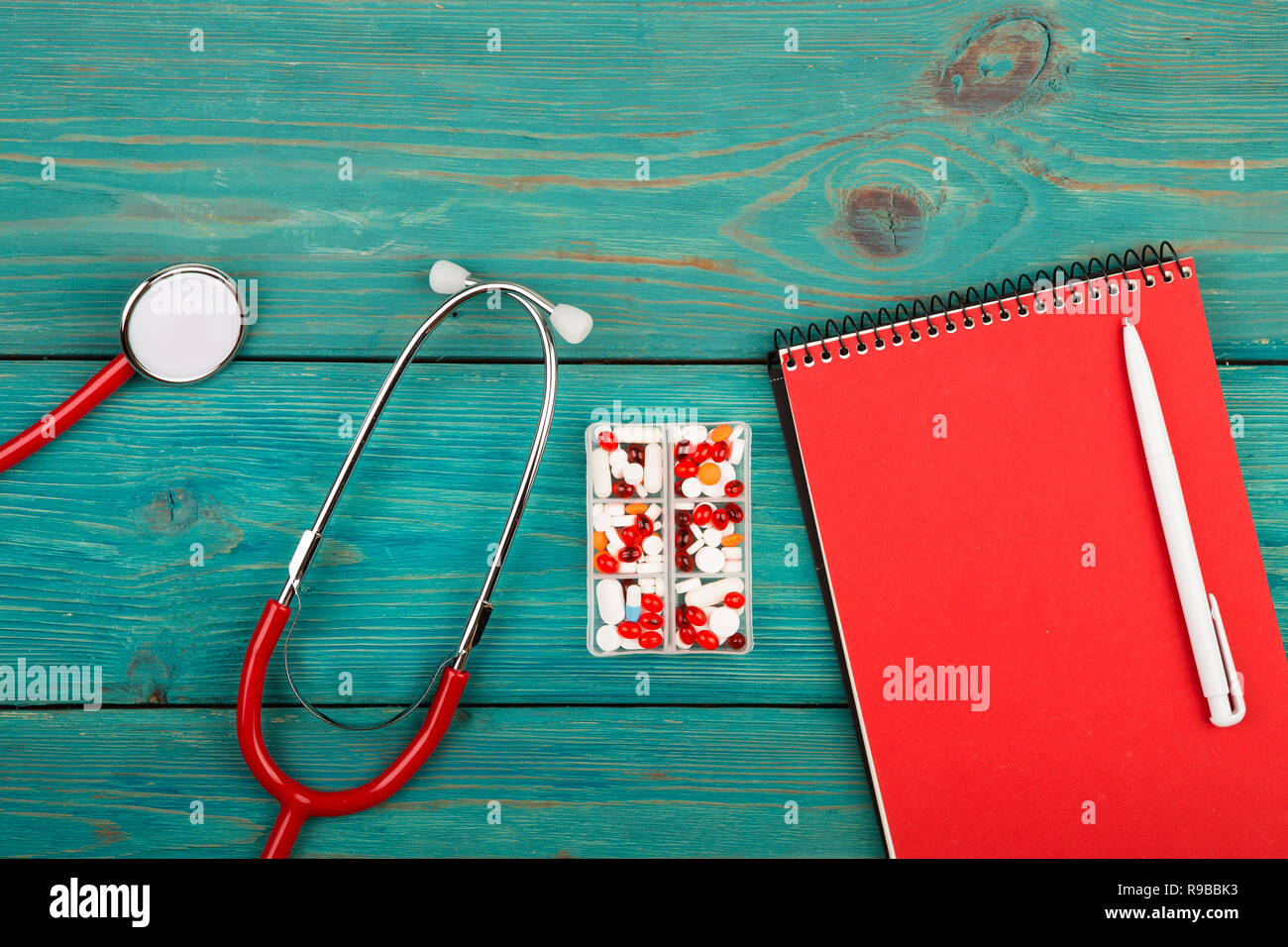 Workplace of a doctor. Red stethoscope, notepad and pills on blue ...