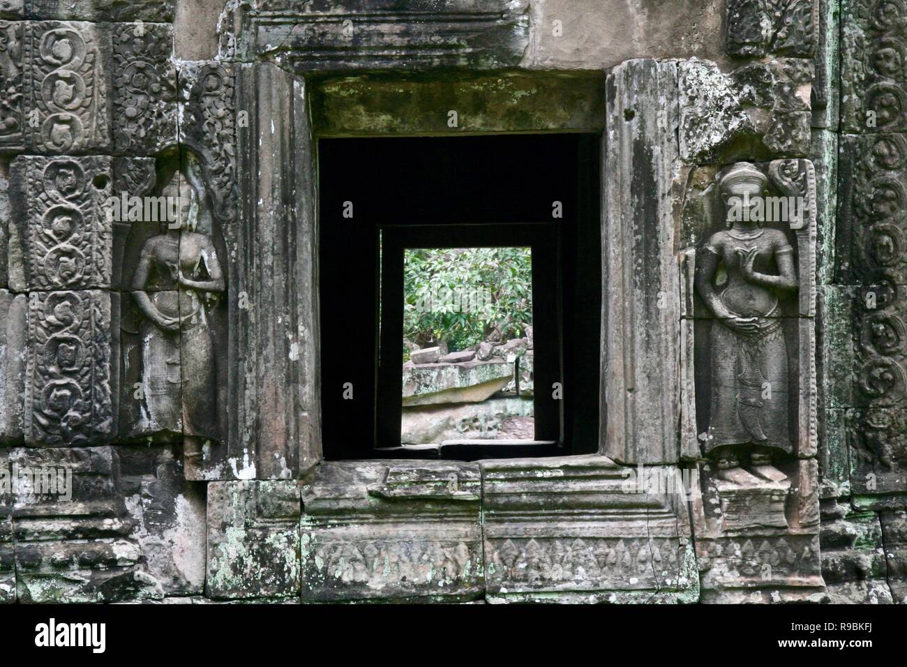 Looking through a window with carved figures either side in Cambodian ...