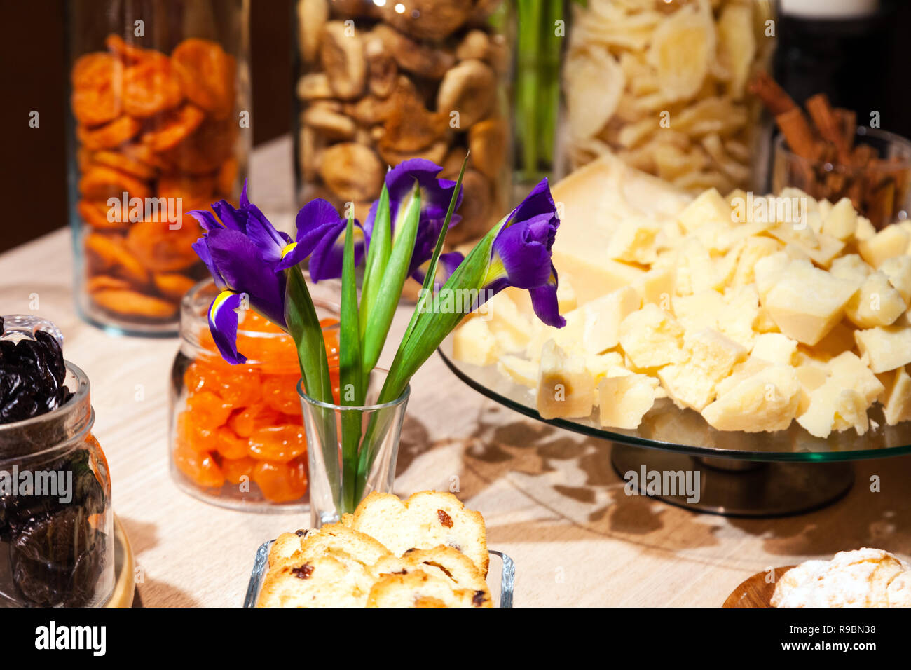 Closeup snacks, dried fruits and nuts in glass bowl, flowers irises in ...
