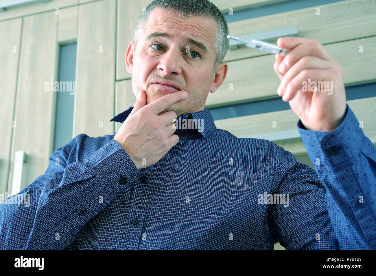 A man holding a thermometer in his hands, measuring body temperature ...