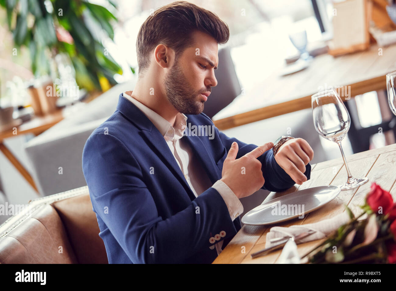 Young man on date in restaurant sitting at table with red rose bouquet ...