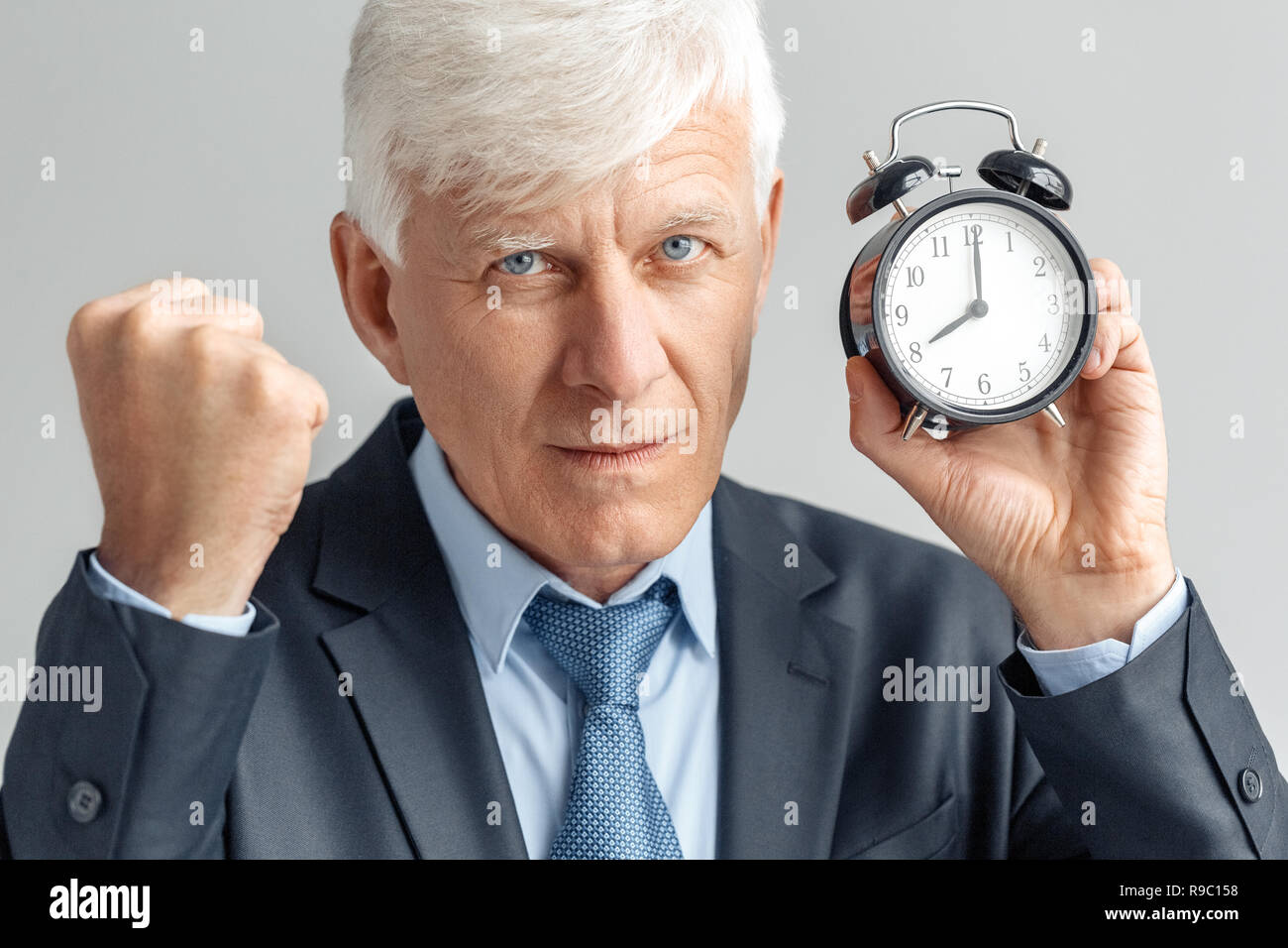 Senior business man studio standing isolated on gray wall holding alarm ...