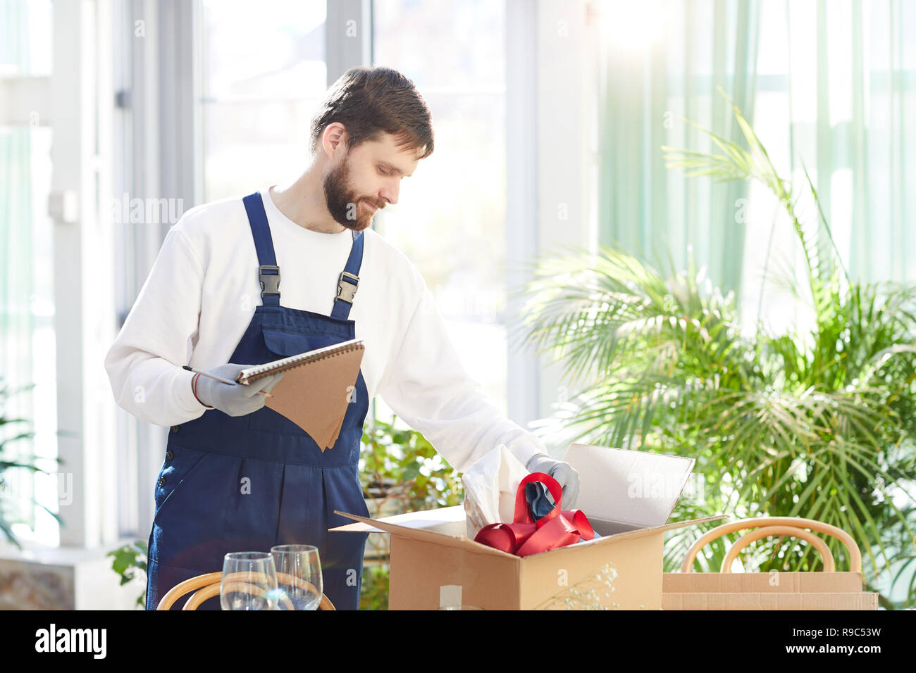 Content moving company worker examining goods in box Stock Photo - Alamy