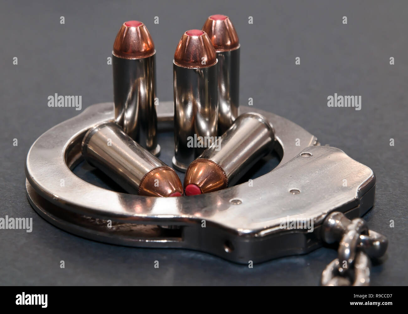 Five 44spl red tipped bullets inside of a metal handcuff on a gray ...