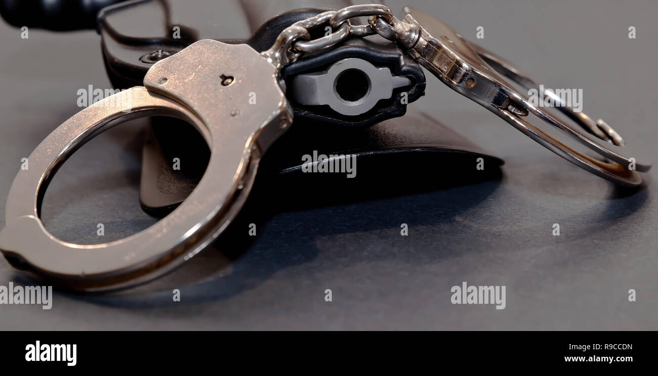 A set of handcuffs on top of a holstered stainless revolver on a gray ...