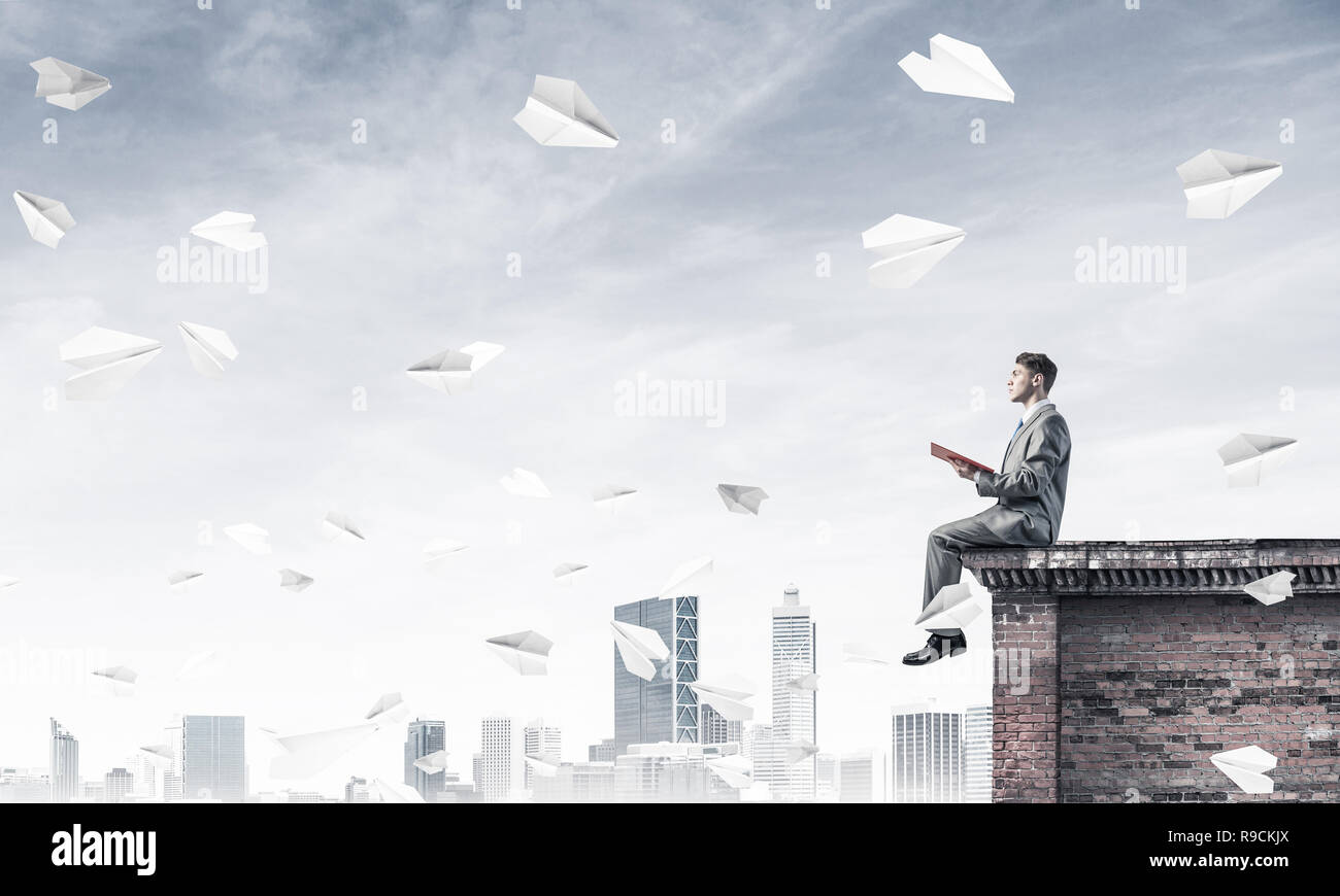Man on roof edge reading book and cityscape at background Stock Photo ...