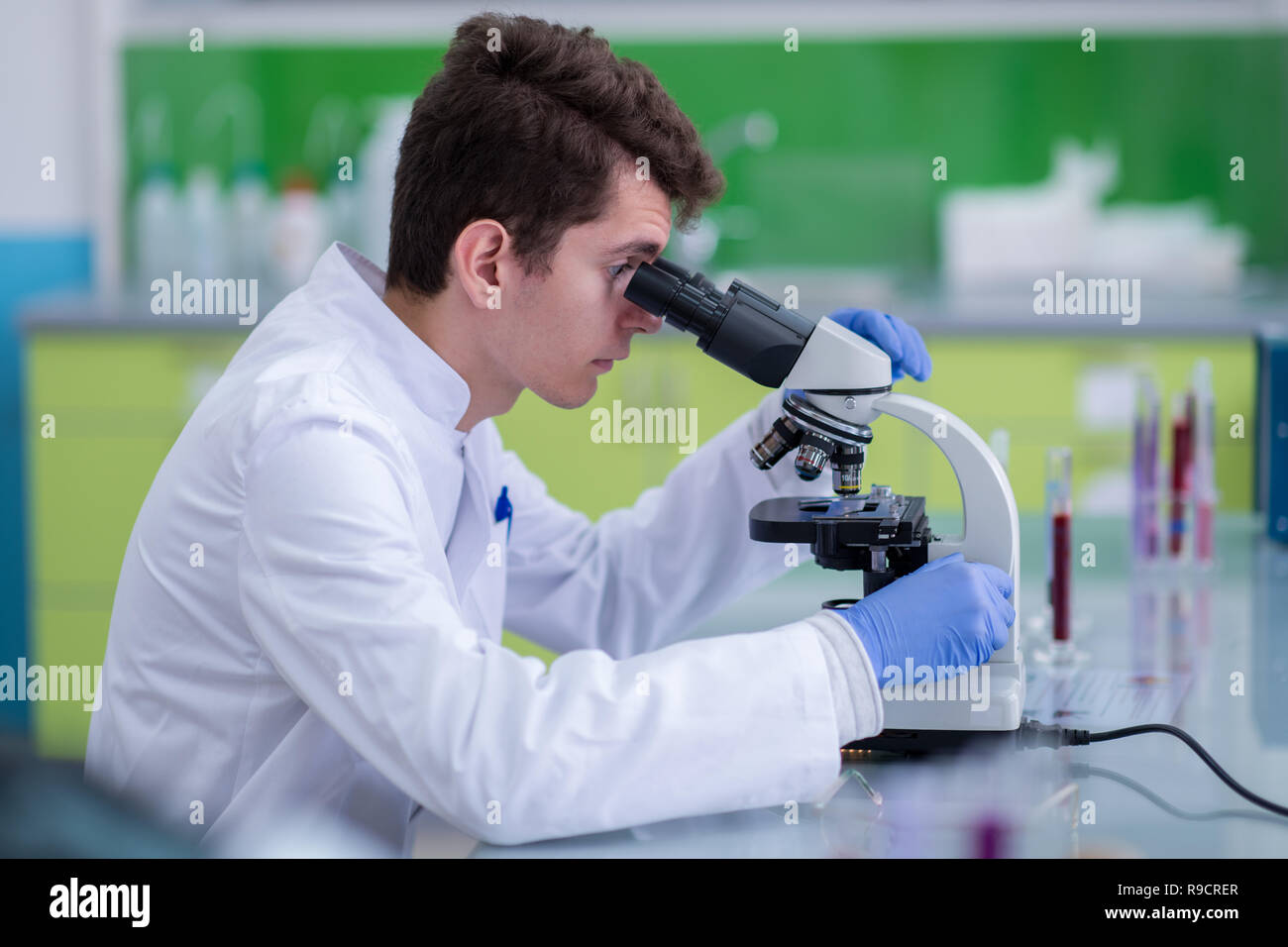 Young student scientist looking through a microscope while doing some ...
