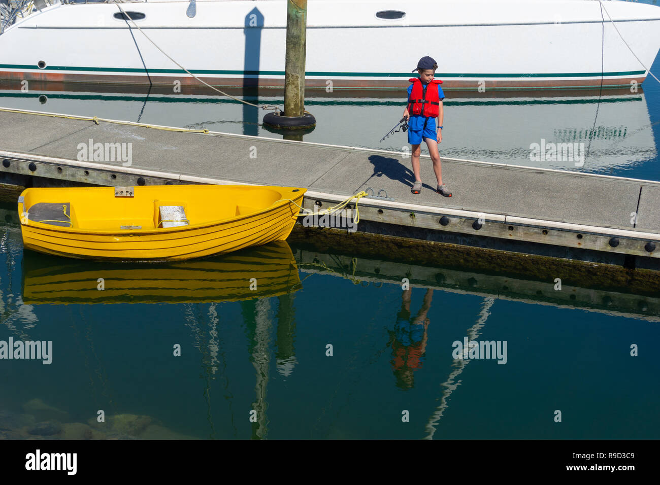 Small boy of marina pier fishingy yellow dinghy reflected in water ...