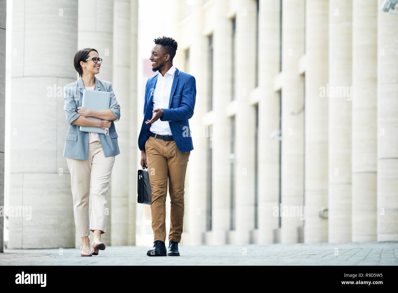 Happy office colleagues talking when walking Stock Photo - Alamy