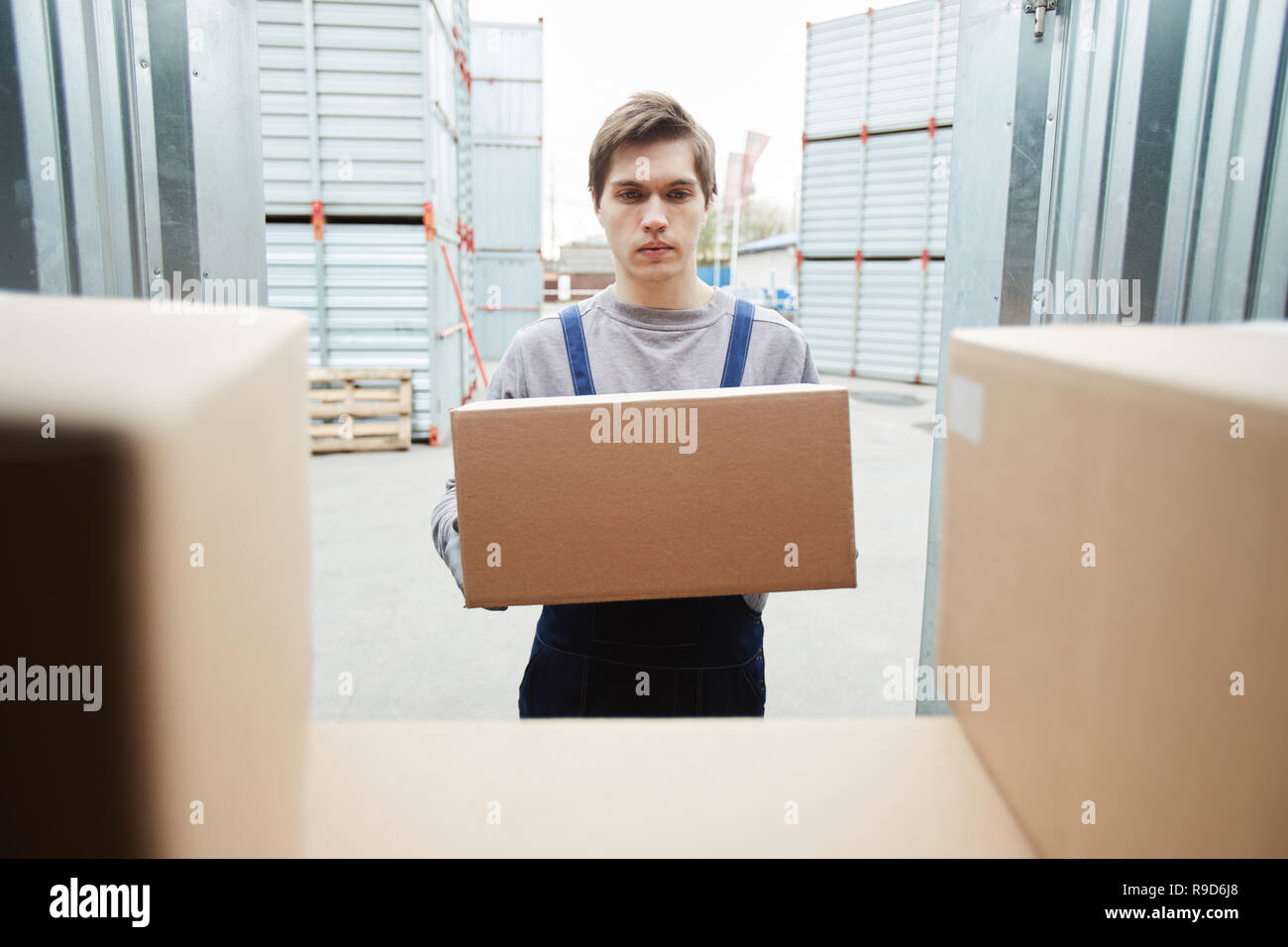 Young worker putting box in container Stock Photo - Alamy