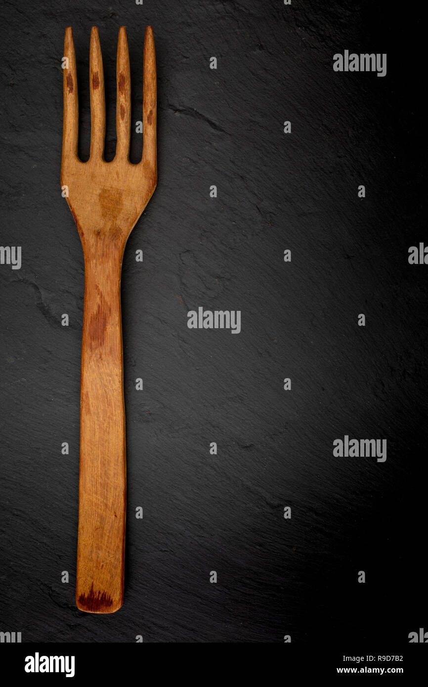 Wooden fork on black slate background with texture. Space to insert ...