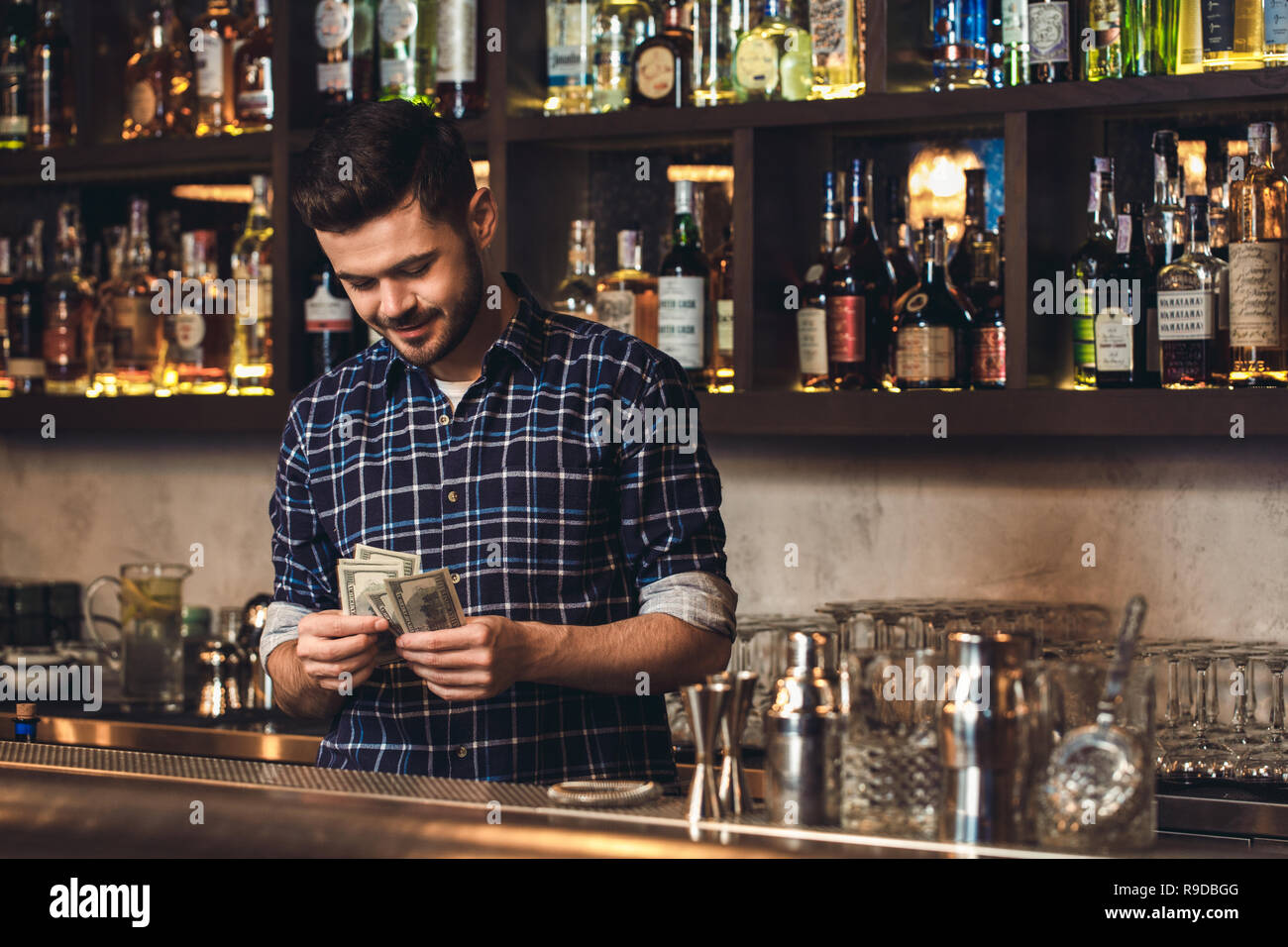 Young barman standing at bar counter counting money monthly salary ...